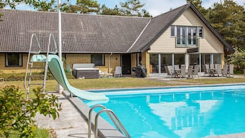 Um imóvel residencial com piscina, escorrega e área de pátio com mobiliário de exterior.
