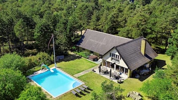 Uma casa de dois andares com piscina, cercada por uma floresta densa.