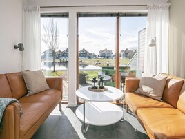 Uma sala de estar moderna com dois sofás de couro, uma mesa de centro branca e vista para uma área residencial através de grandes portas de vidro.