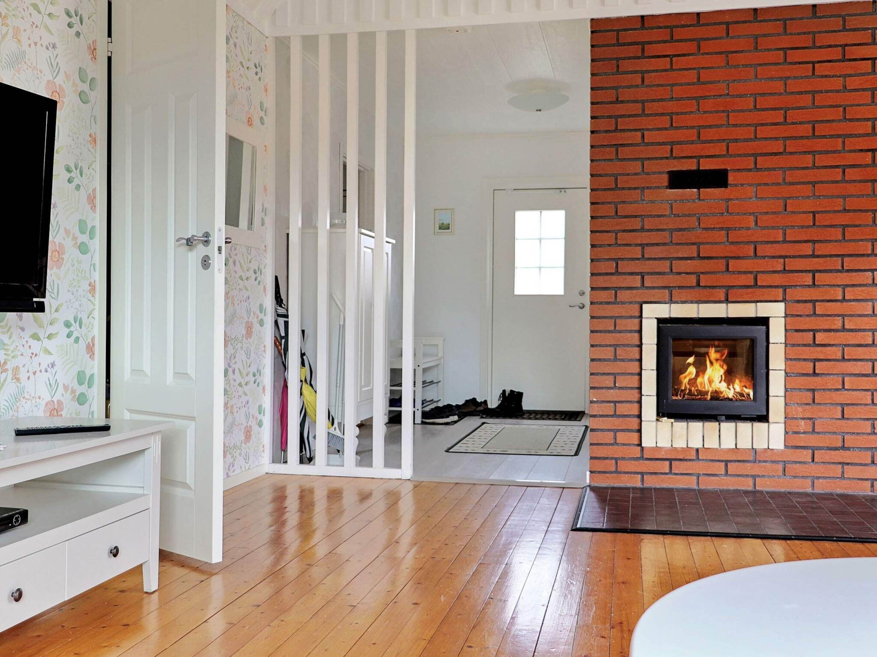 Quarto com lareira, piso de madeira, um móvel de entretenimento branco e porta que dá para outro cômodo.