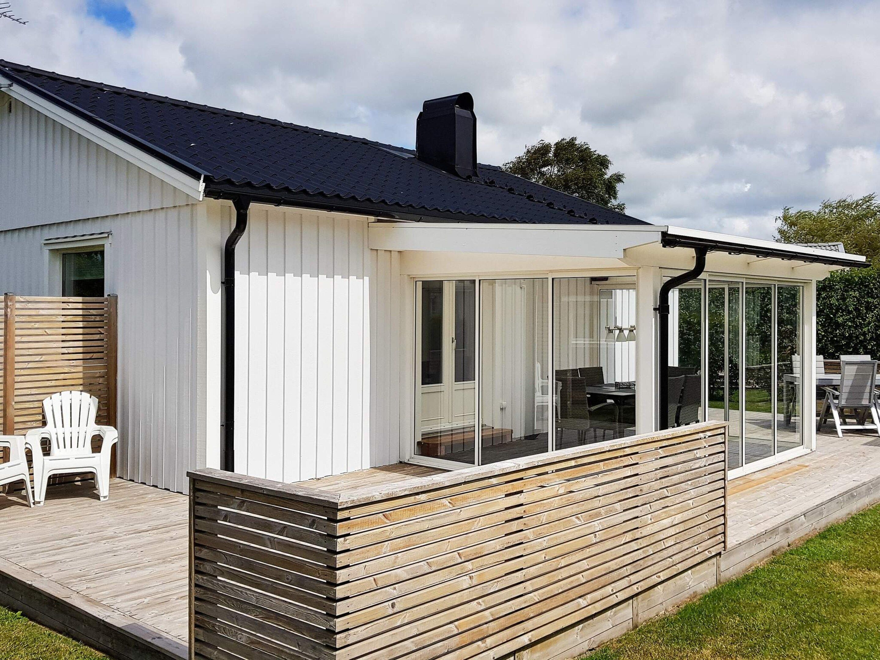 Uma casa moderna com varanda coberta, chaminé e deck com cadeiras.