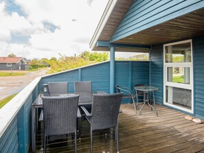 Uma área externa coberta com mesa, cadeiras, uma janela e vista para o bairro ao redor.
