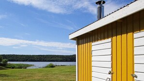 Um edifício com porta amarela e chaminé, com vista para um lago e uma floresta.