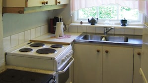 Cozinha compacta com fogão, pia e janela com cortinas.