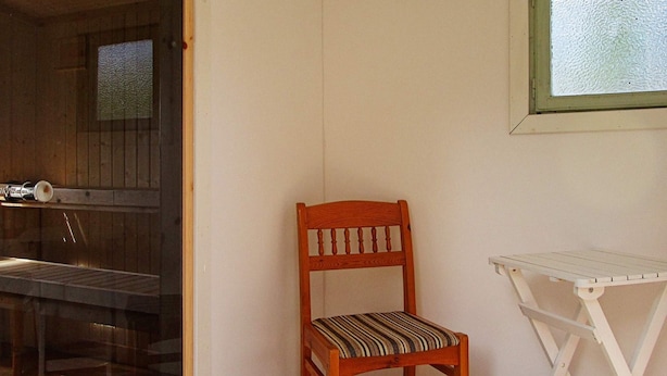 Uma cadeira de madeira com almofada listrada num canto de um quarto com paredes brancas e chão de madeira.