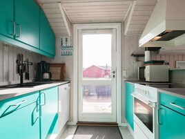 Cozinha com armários verde-água, uma porta branca e vista para um edifício vermelho lá fora.