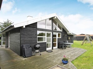 Uma casa moderna com um terraço, churrasqueira e jardim.