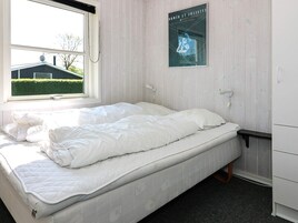 Quarto individual com uma cama, janela, um cartaz na parede e mesa de cabeceira.
