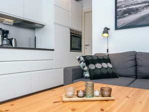 Cozinha moderna com armários brancos, máquina de café e área de refeições com mesa de madeira e sofá cinza.