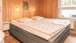 Quarto com painéis de madeira, uma cama, duas luzes fixadas na parede e uma janela.