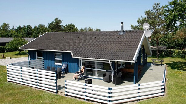 Um edifício azul com telhado inclinado, área coberta para refeições ao ar livre e uma mesa de piquenique.
