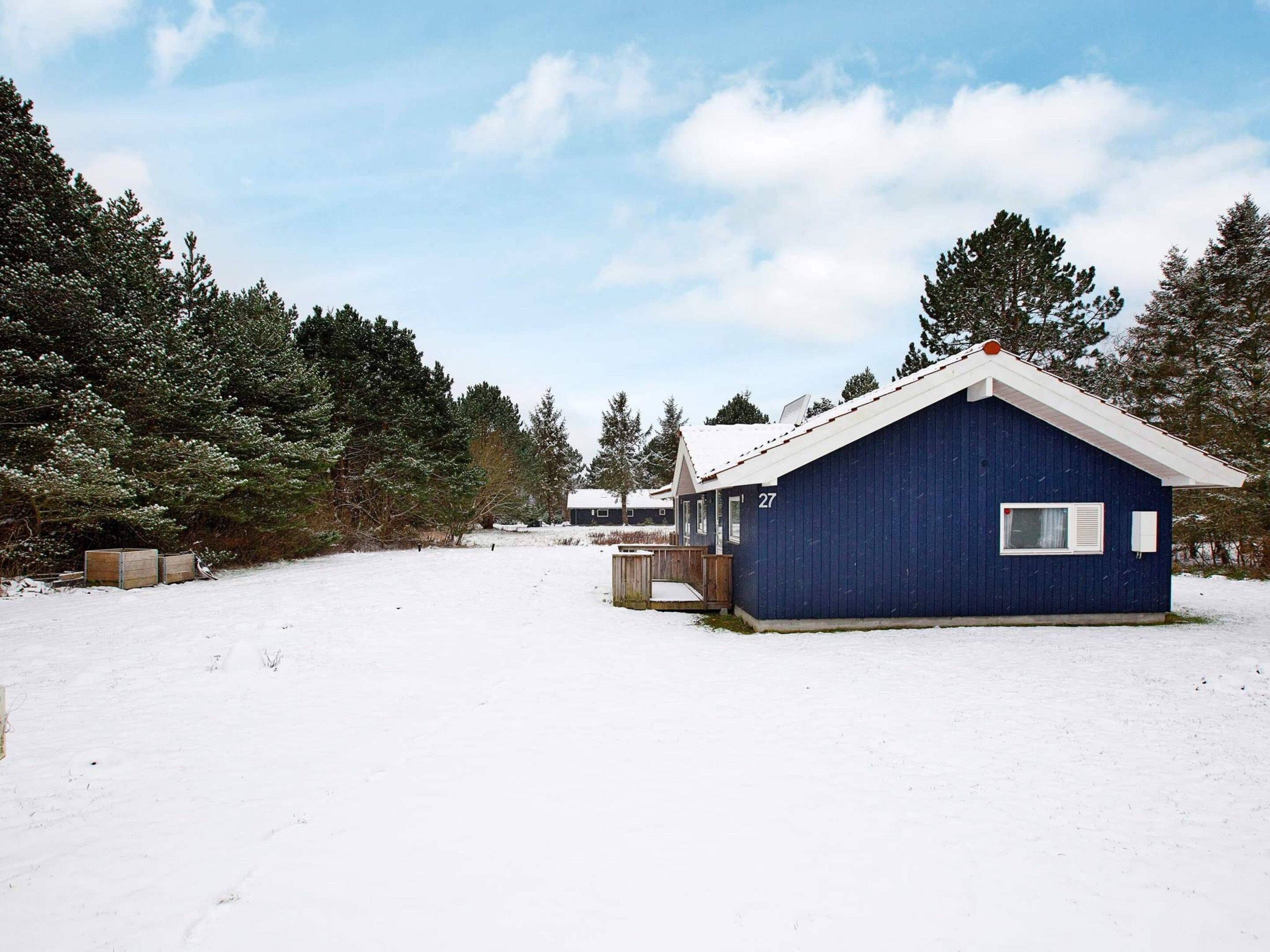 Paisagem coberta de neve com uma cabana azul e um edifício menor, rodeados por árvores.