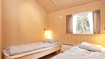 Quarto com duas camas, paredes de madeira, uma janela com cortinas e um aplique de parede.