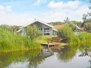 Uma casa com telhado inclinado, um deck e um lago na frente.