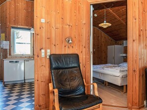 Quarto com poltrona de couro preto, cama, teto de madeira e janela com vista para árvores.
