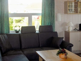 Sala de estar com sofá, mesa com planta, armário com copos e janela com cortinas.