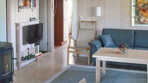 Uma sala de estar com televisão, sofá, mesa e uma cadeira.
