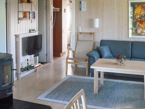 Uma sala de estar com televisão, sofá, mesa e uma cadeira.