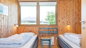 Quarto com duas camas, um banco de madeira e janela com vista para o verde.