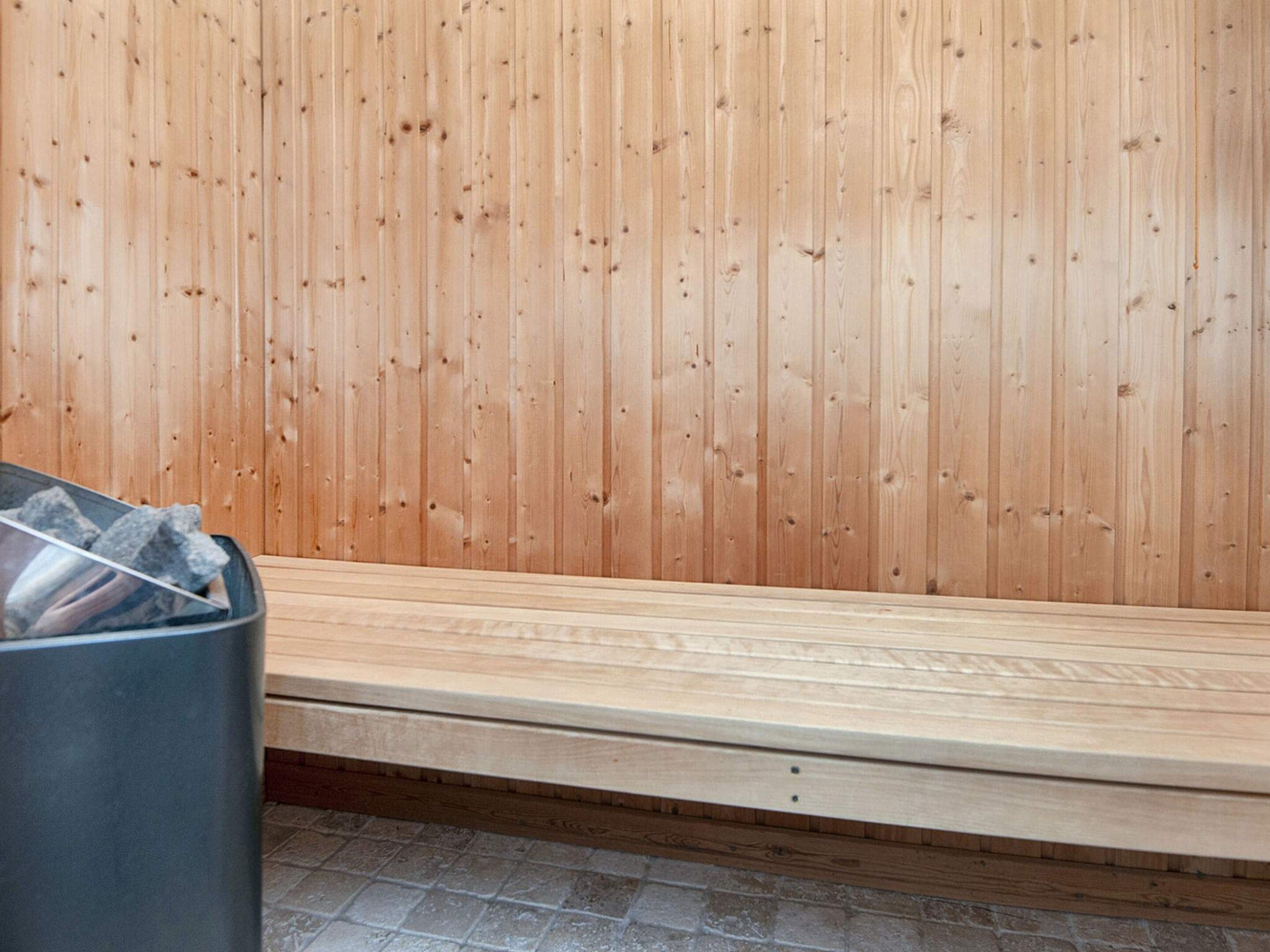 Uma sauna com banco de madeira e uma lixeira.