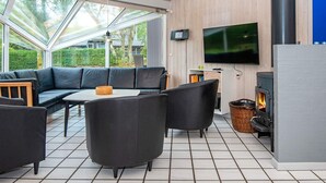Um espaço ao ar livre moderno com área envidraçada, sofá de couro preto, mesa de jantar e lareira.