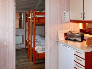 Quarto compacto com beliche, cozinha compacta com torradeira e armário de madeira.