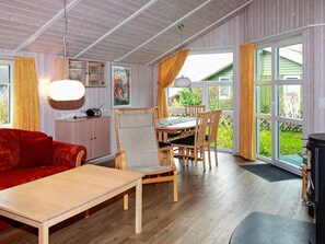 Quarto com mesa de jantar de madeira, cadeiras, sofá, armário e uma janela grande com cortinas.