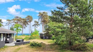 Uma cabana com varanda e área de estar ao ar livre, cercada por árvores e vista para o oceano.