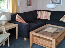 Uma sala de estar com um sofá escuro, almofadas listradas, uma mesa de centro de vidro, uma mesinha de cabeceira de madeira e uma cadeira.