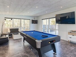 Uma sala de estar moderna com mesa de bilhar, um sofá e uma televisão.