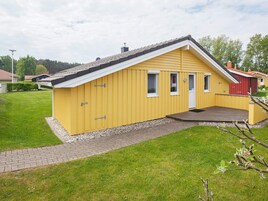 Um edifício amarelo com telhado inclinado, varanda frontal e um pequeno jardim.