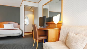 Quarto de hotel com cama, escrivaninha com computador, cadeira, sofá, espelho e abajur.