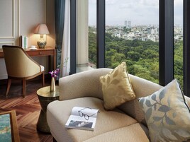 Uma sala de estar moderna com sofá, mesa lateral, luminária e vista para um horizonte urbano através de grandes janelas.