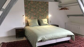 Um quarto com uma cama, duas mesinhas de cabeceira, um criado-mudo e um guarda-roupa, com papel de parede estampado com flores.
