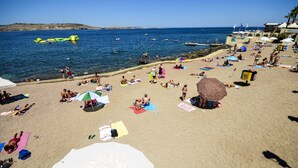 Uma praia com pessoas tomando sol, guarda-sóis e uma torre de salva-vidas.