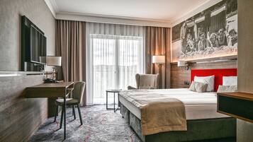 Quarto de hotel com cama, escrivaninha, cadeira e televisão.
