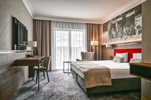 Quarto de hotel com cama, escrivaninha, cadeira e televisão.