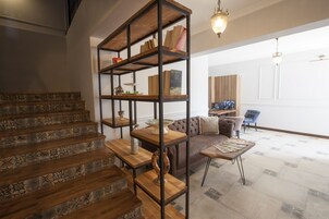 Uma escadaria com ladrilhos estampados, uma estante de madeira, um sofá de couro e uma mesa de centro em um ambiente bem iluminado com uma janela grande.