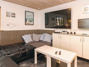 Uma sala de estar moderna com sofá, mesa de centro, televisão e área de cozinha com armários e relógio.