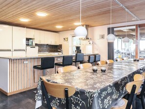 Cozinha moderna com ilha central, área de jantar com mesa comprida e iluminação pendente.