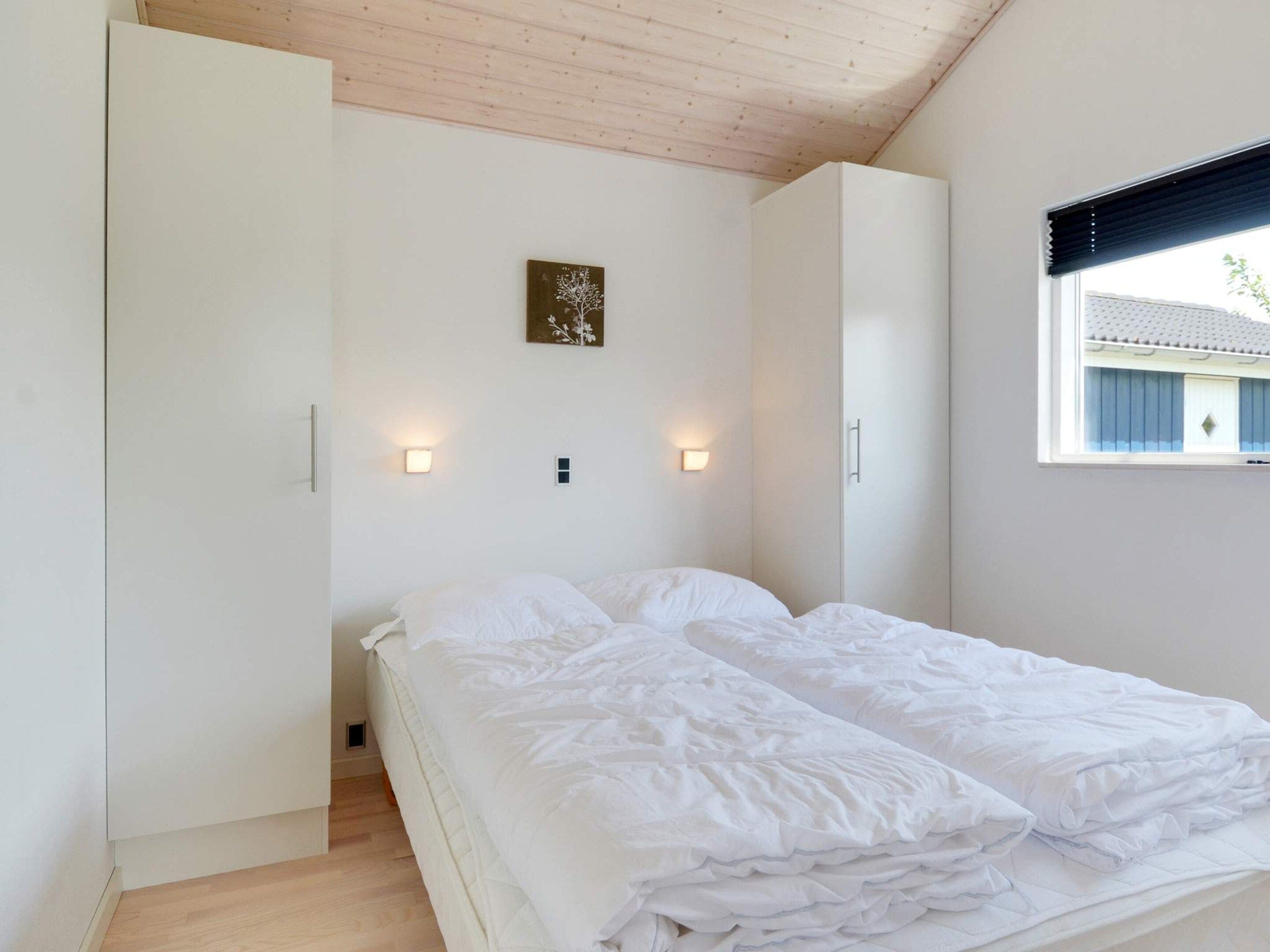 Quarto com cama, duas luminárias na parede, uma janela e uma porta.