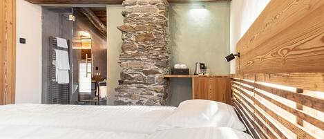 Quarto com um pilar de pedra, cabeceira de madeira e cama com roupa de cama branca.