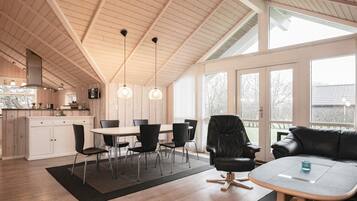 Ampla sala de estar com mesa e cadeiras para refeições, um sofá de couro preto e uma grande janela com vista para o exterior.
