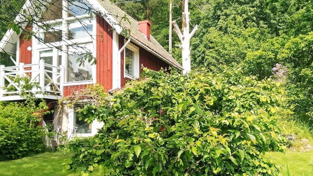 Uma casa vermelha com detalhes brancos, rodeada por arbustos verdes exuberantes e um gramado bem cuidado.