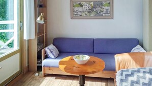Um quarto com um sofá azul, uma pequena mesa de madeira com uma tigela, uma luminária e uma imagem de um panorama urbano emoldurada na parede.