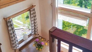Uma mesa de jantar de madeira com um vaso de flores, uma janela com cortinas e vista para o verde lá fora.