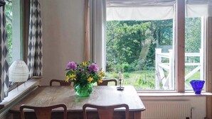Uma mesa de jantar com quatro cadeiras, um vaso com flores e vista para o verde lá fora.