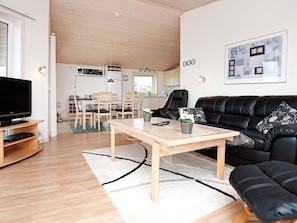Uma sala de estar moderna com televisão de tela plana, um sofá de couro preto, uma mesa de centro de madeira e uma área de jantar com cadeiras e mesa de madeira.