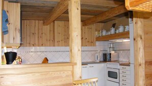 Interior em madeira com cozinha, incluindo armários, fogão e mesa de jantar com uma cadeira.