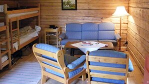 Interior de uma cabana com beliches, um sofá, uma mesa e um abajur.